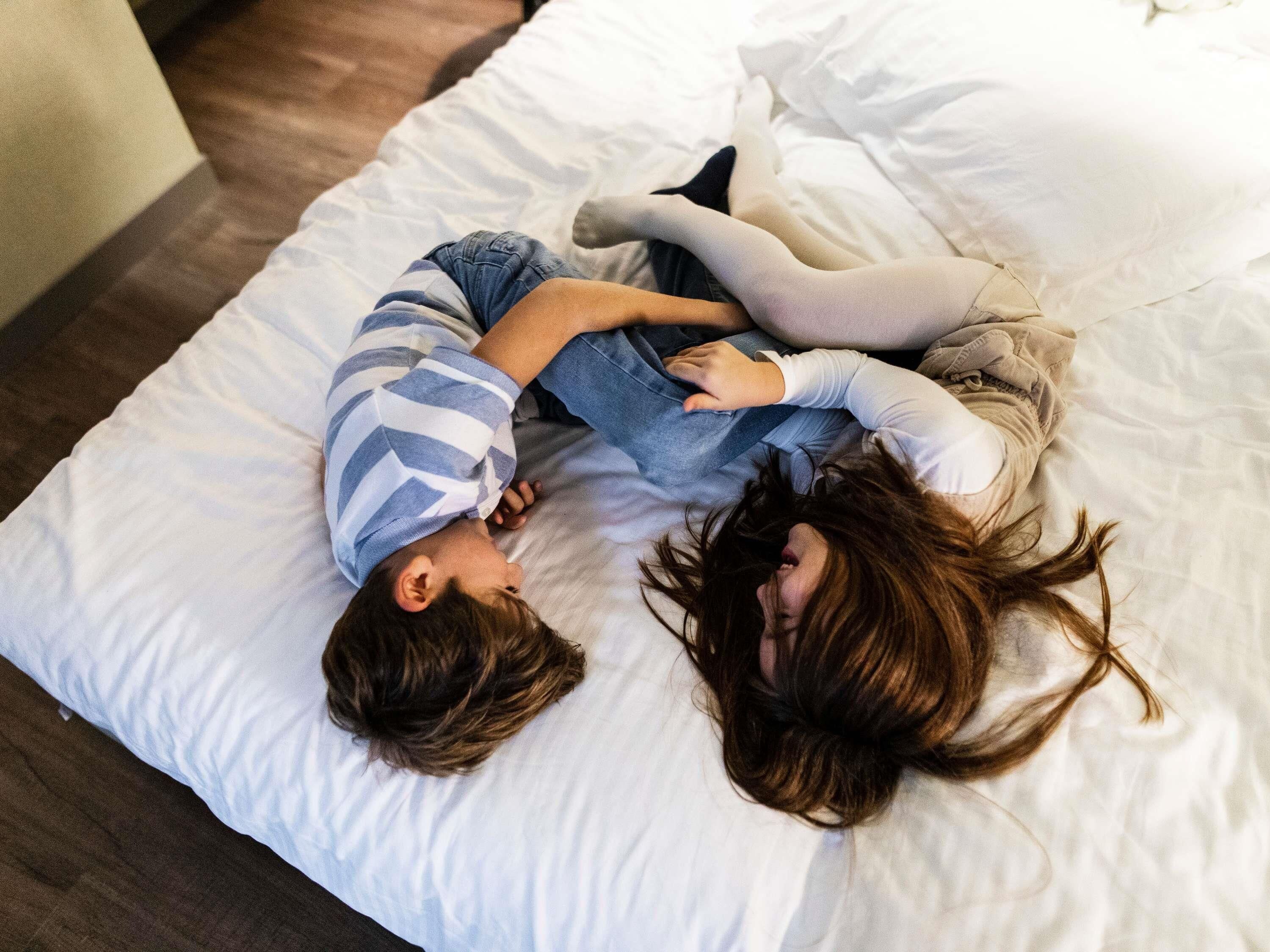 Duas pessoas deitadas em uma cama com lençóis brancos e chão de madeira.