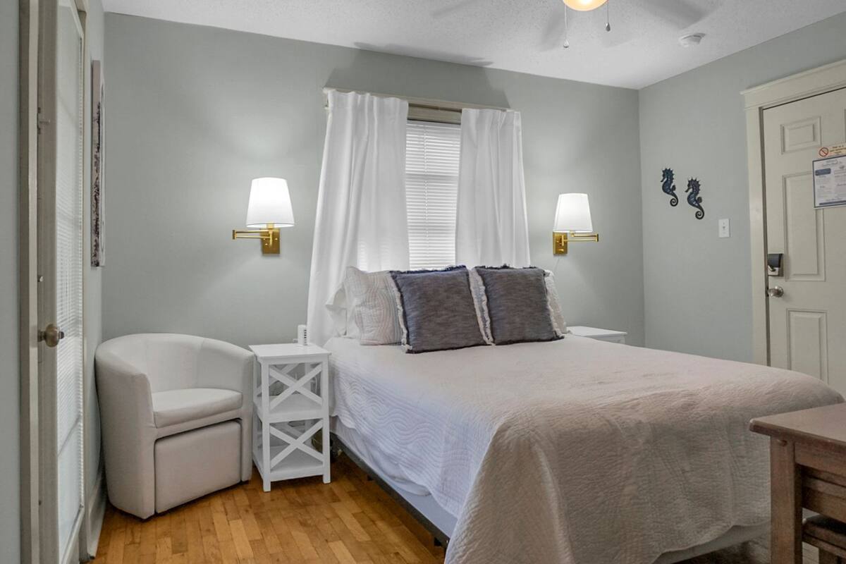 Quarto com cama, duas luminárias de cabeceira, uma cadeira e mesa de cabeceira.
