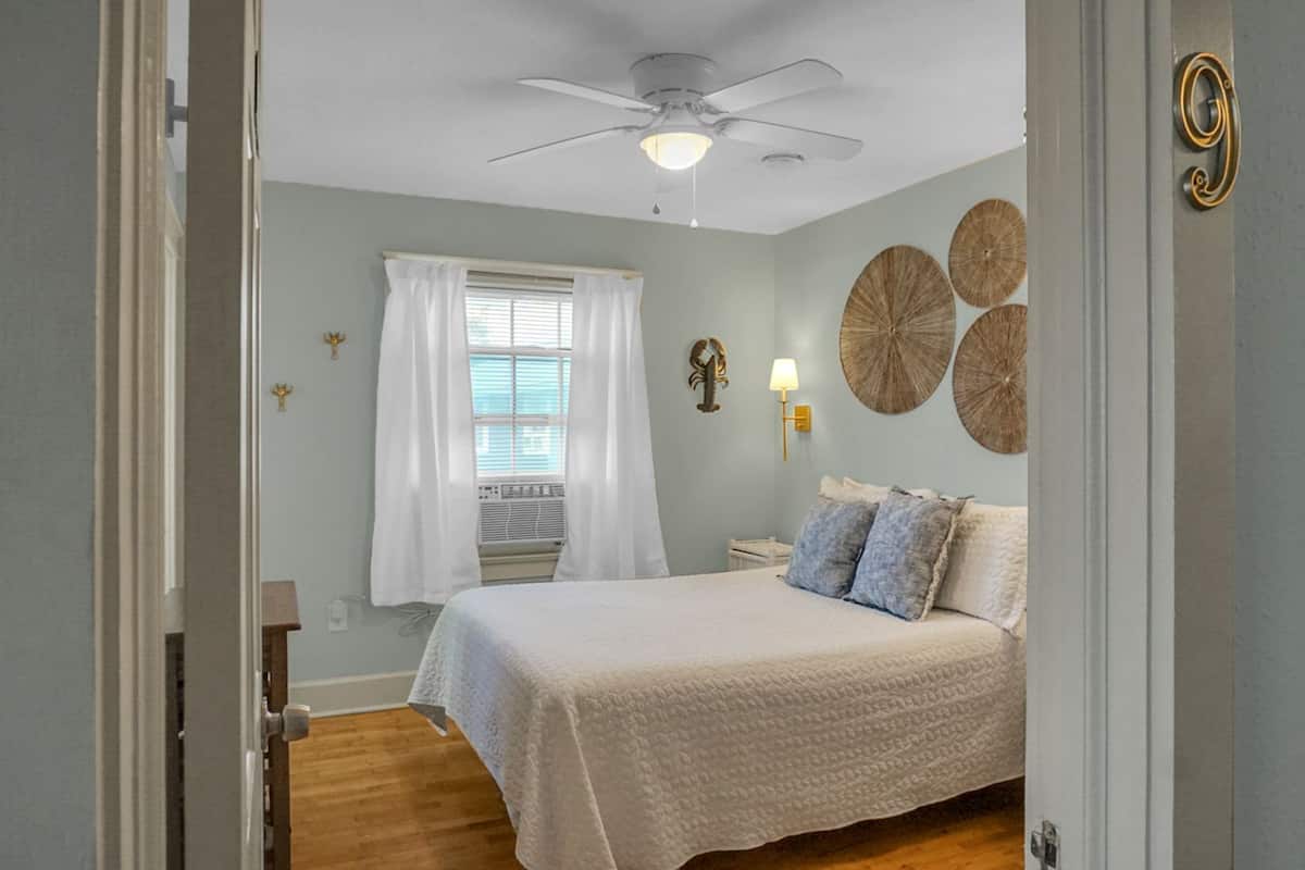 Quarto com cama, ventilador de teto, janela com cortinas e decoração de parede.