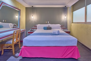 Quarto de hotel com cama, escrivaninha, cadeira, espelho e janela.