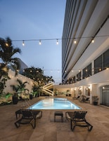 Uma área de piscina com espreguiçadeiras, luzes de festa e uma escadaria para um andar superior.