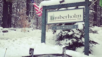 Placa coberta de neve para o Timberholm Inn, com indicação de pousada e café da manhã.