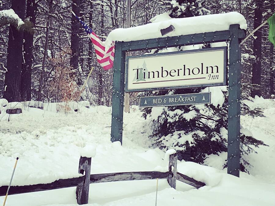Placa coberta de neve para o Timberholm Inn, com indicação de pousada e café da manhã.