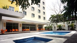 Área de piscina ao ar livre com duas piscinas, cercada por cadeiras laranja e plantas em vasos.