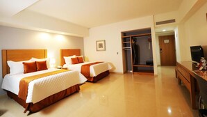 Quarto de hotel com duas camas, uma escrivaninha, uma televisão e um guarda-roupa.