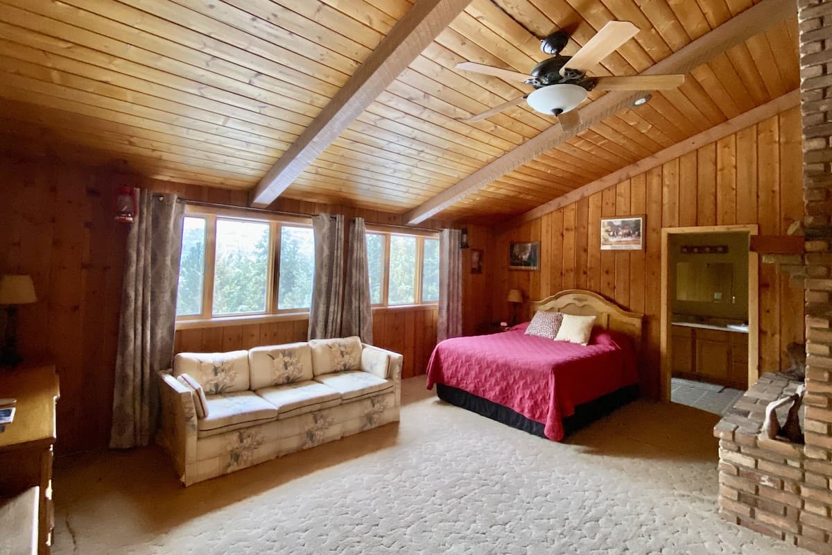 Quarto de cabana de madeira com cama, sofá, ventoinha no teto e lareira.