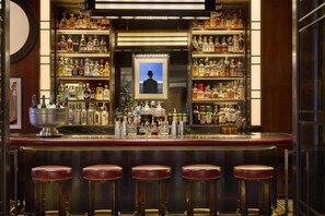 Uma área de bar com várias prateleiras de garrafas de bebidas, um quadro e banquetas.