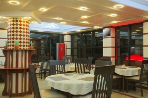 Um restaurante com mesas redondas, cadeiras e um pilar decorativo.