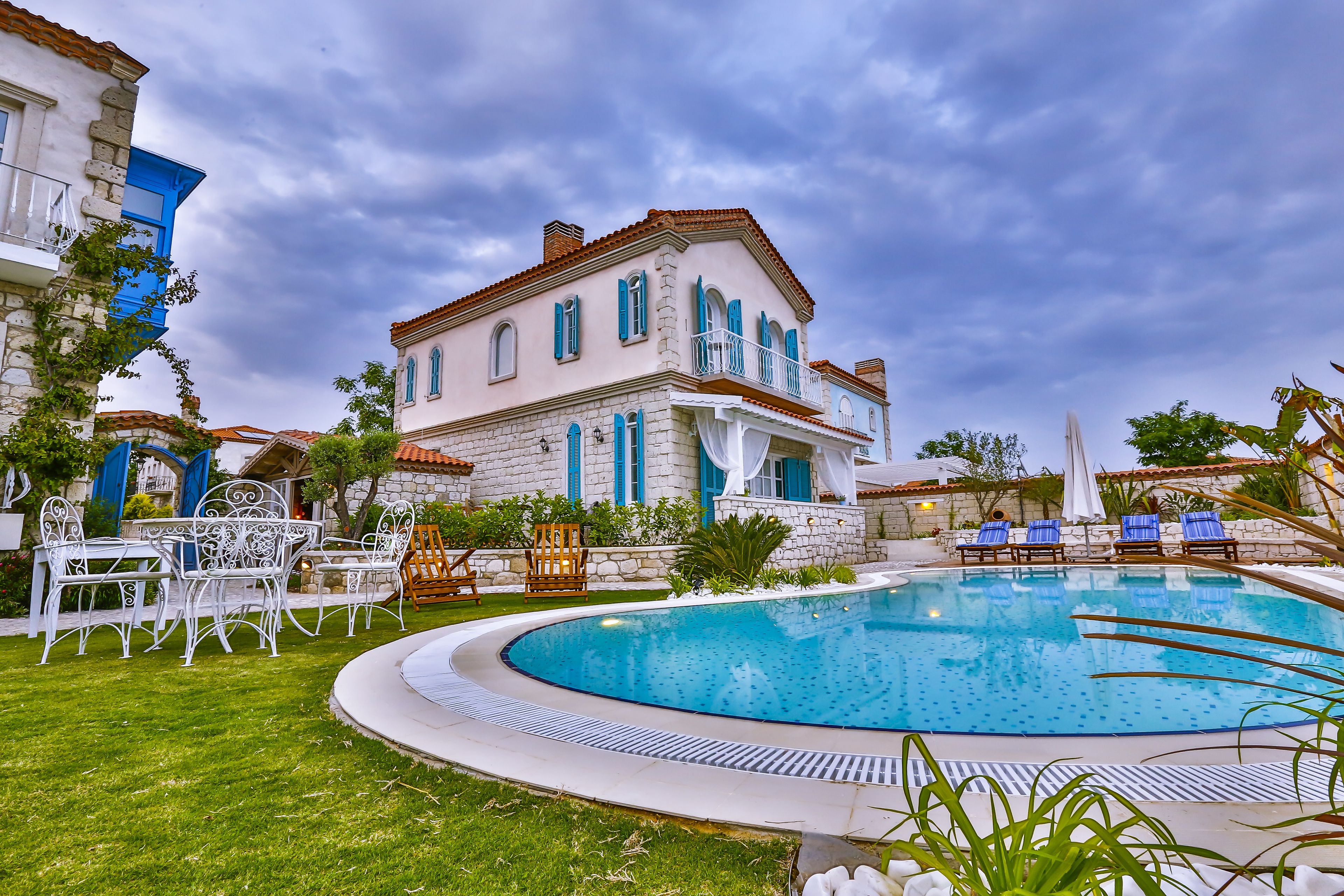 Uma área de piscina com uma piscina grande, cadeiras de descanso e um edifício com persianas azuis.