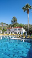 Uma área de piscina com cadeiras de descanso amarelas e guarda-sóis, um edifício com varandas e palmeiras.