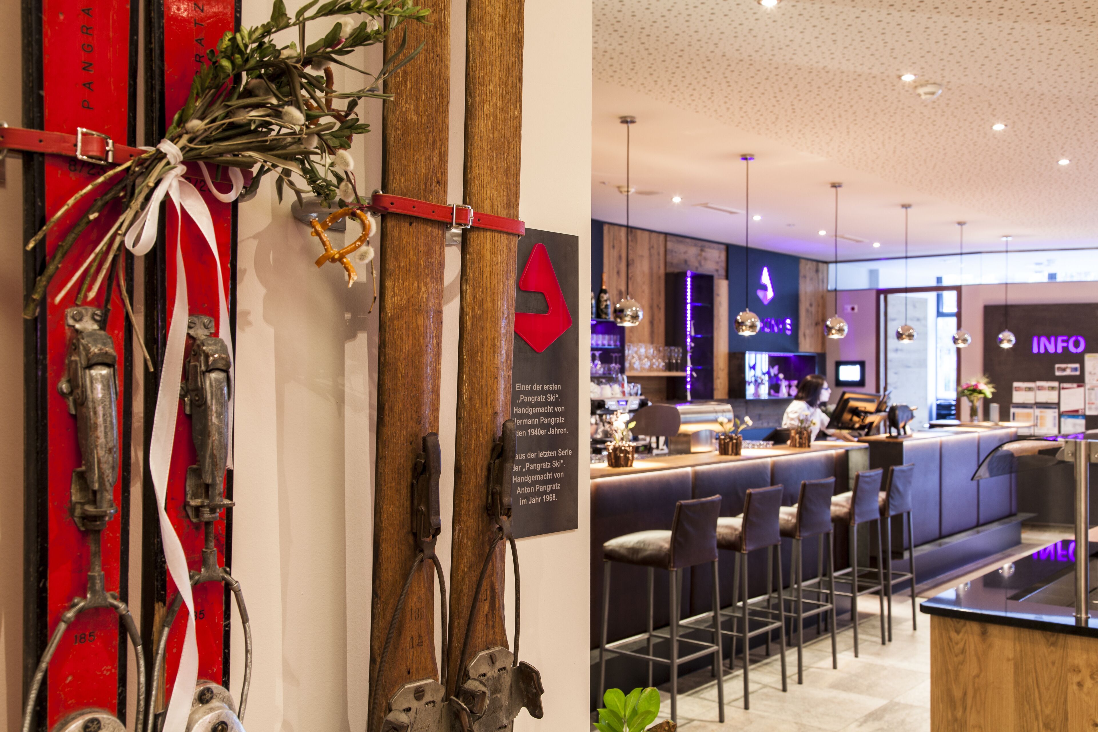 Uma área de bar moderna com balcão, banquetas e um arranjo decorativo de esquis e folhagem.