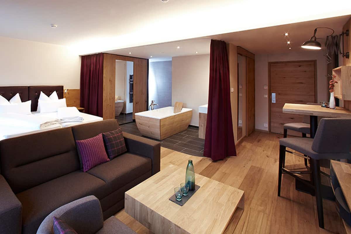 Quarto de hotel moderno com uma cama grande, um sofá, uma mesa de centro e um espaço para refeições.