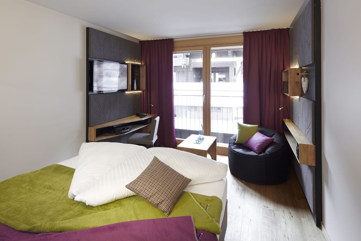 Quarto de hotel com cama, escrivaninha, cadeira, sofá e televisão.