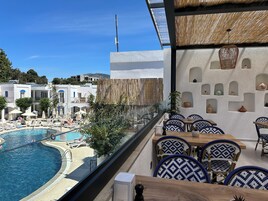 Área à beira da piscina com vista para uma praia e edifícios. Há espreguiçadeiras e uma mesa com cadeiras.