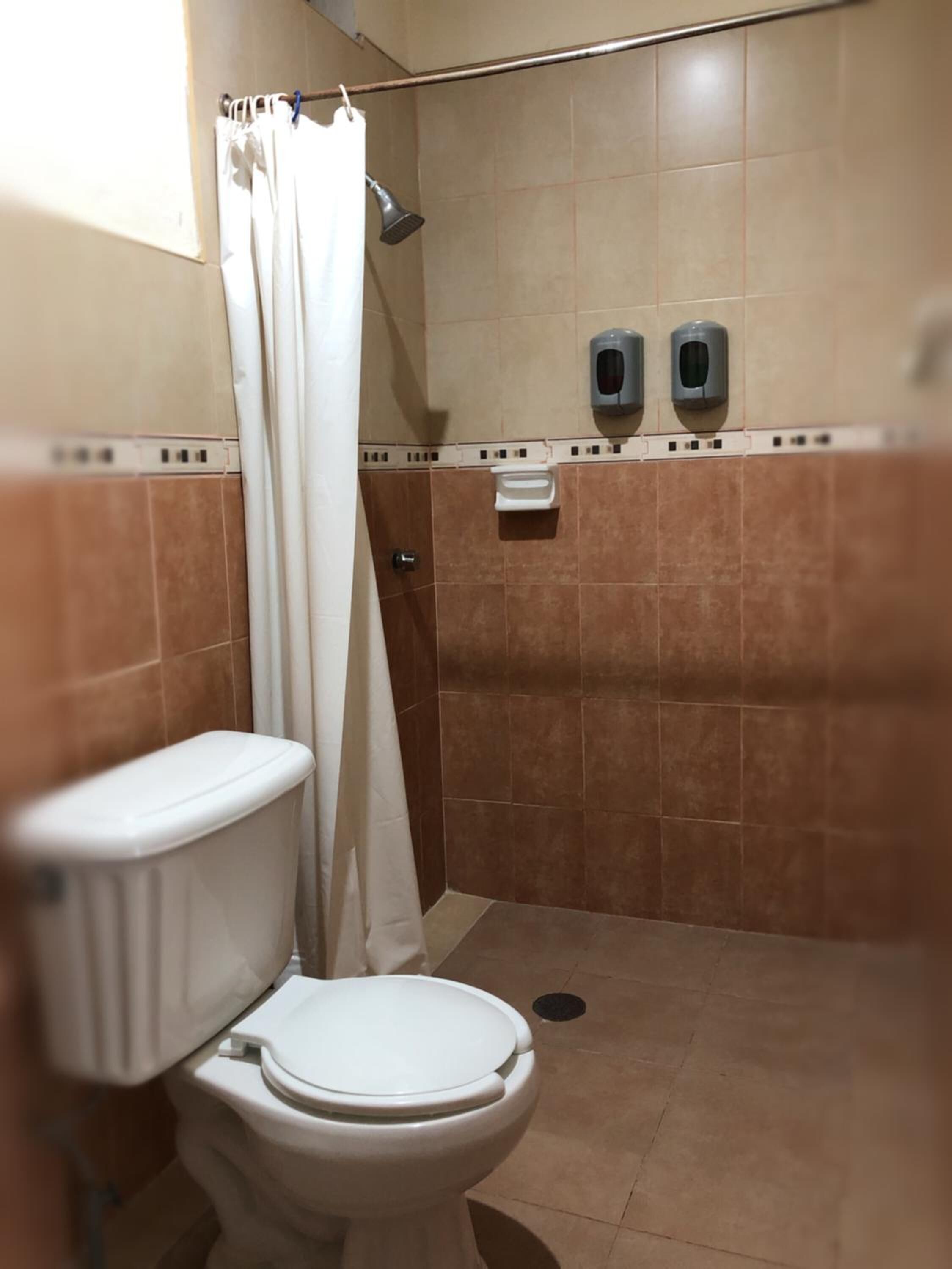 Casa de banho com sanita, cortina de chuveiro e dois dispensadores de sabonete na parede.