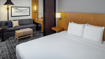 Quarto de hotel com cama, sofá, escrivaninha e luminária.