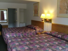 Quarto de hotel com cama, escrivaninha e cadeira. Há duas luminárias na parede e um quadro sobre a cama.