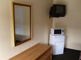 Quarto com penteadeira de madeira, frigorífico branco, micro-ondas e televisão na parede.