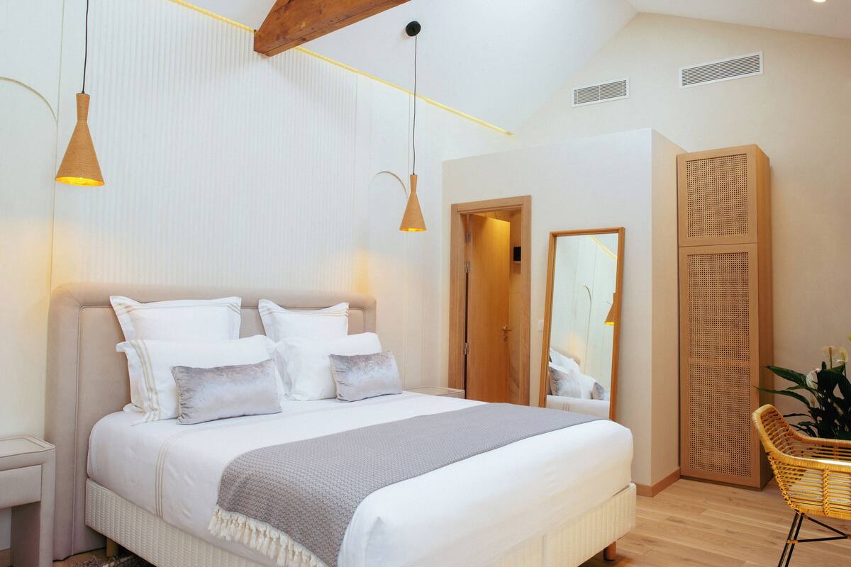 Um quarto moderno com uma cama grande, mesas de cabeceira, um guarda-roupa de madeira e uma cadeira de vime.