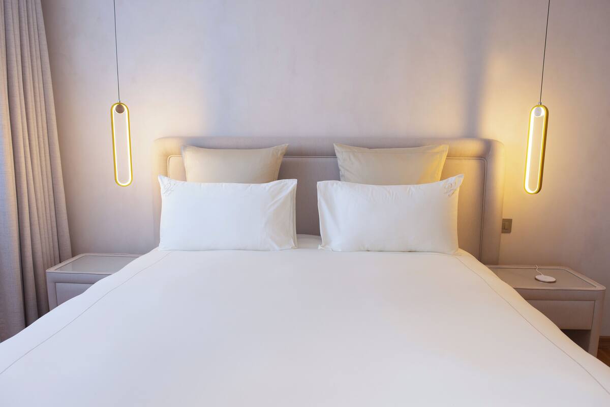 Quarto de hotel moderno com uma cama grande, duas mesas de cabeceira e um candeeiro suspenso.