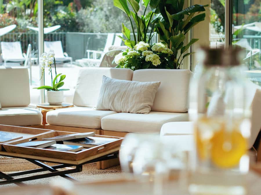 Uma sala de estar moderna com um sofá, uma mesa de centro e uma janela grande com vista para móveis de exterior e vegetação.