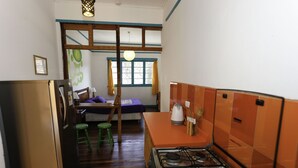 Cozinha compacta com fogão a gás, banquetas de madeira, uma pequena mesa de jantar e uma janela com cortinas.
