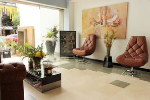 Um hall moderno com poltronas de couro, uma mesa de centro de vidro com flores, uma adega e um grande quadro abstrato na parede.