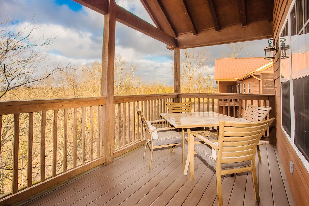 Um deck de madeira com mesa e cadeiras, com vista para uma paisagem natural.