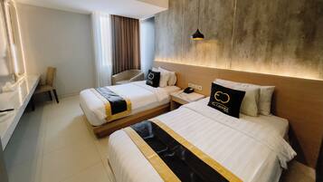 Quarto de hotel com duas camas, uma escrivaninha, uma cadeira e um espelho grande.