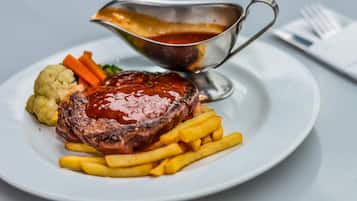 Um prato com bife, batatas fritas e legumes, e um regador de molho.