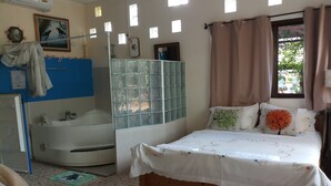 Quarto com cama, banheira, janela com cortinas e banheiro com toalha pendurada.