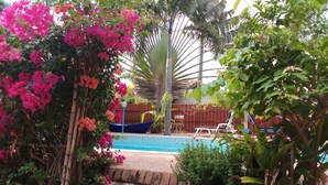 Uma área de piscina com degraus que levam à água, rodeada por vegetação exuberante e plantas floridas.