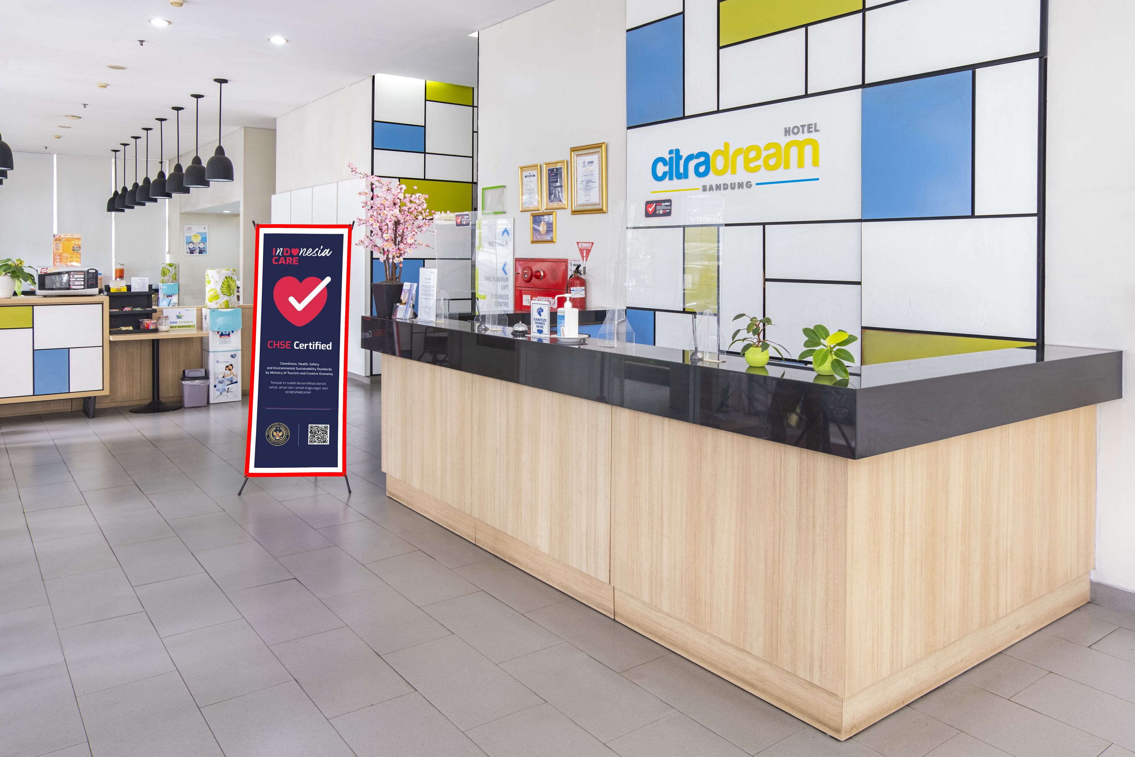 Uma área de recepção de hotel com design moderno, apresentando um balcão de atendimento, um selo CHSE Certified e uma placa 'citradream' na parede.