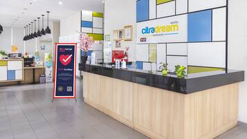 Uma área de recepção de hotel com design moderno, apresentando um balcão de atendimento, um selo CHSE Certified e uma placa 'citradream' na parede.