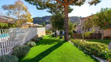 Um jardim bem cuidado com piscina, uma grande árvore e um edifício de fachada branca.