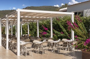 Área de pátio externo com mesas e cadeiras, cercada por vegetação e flores.