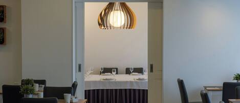Uma sala de jantar moderna com uma mesa posta para dois, uma luminária pendente decorativa e cadeiras pretas.