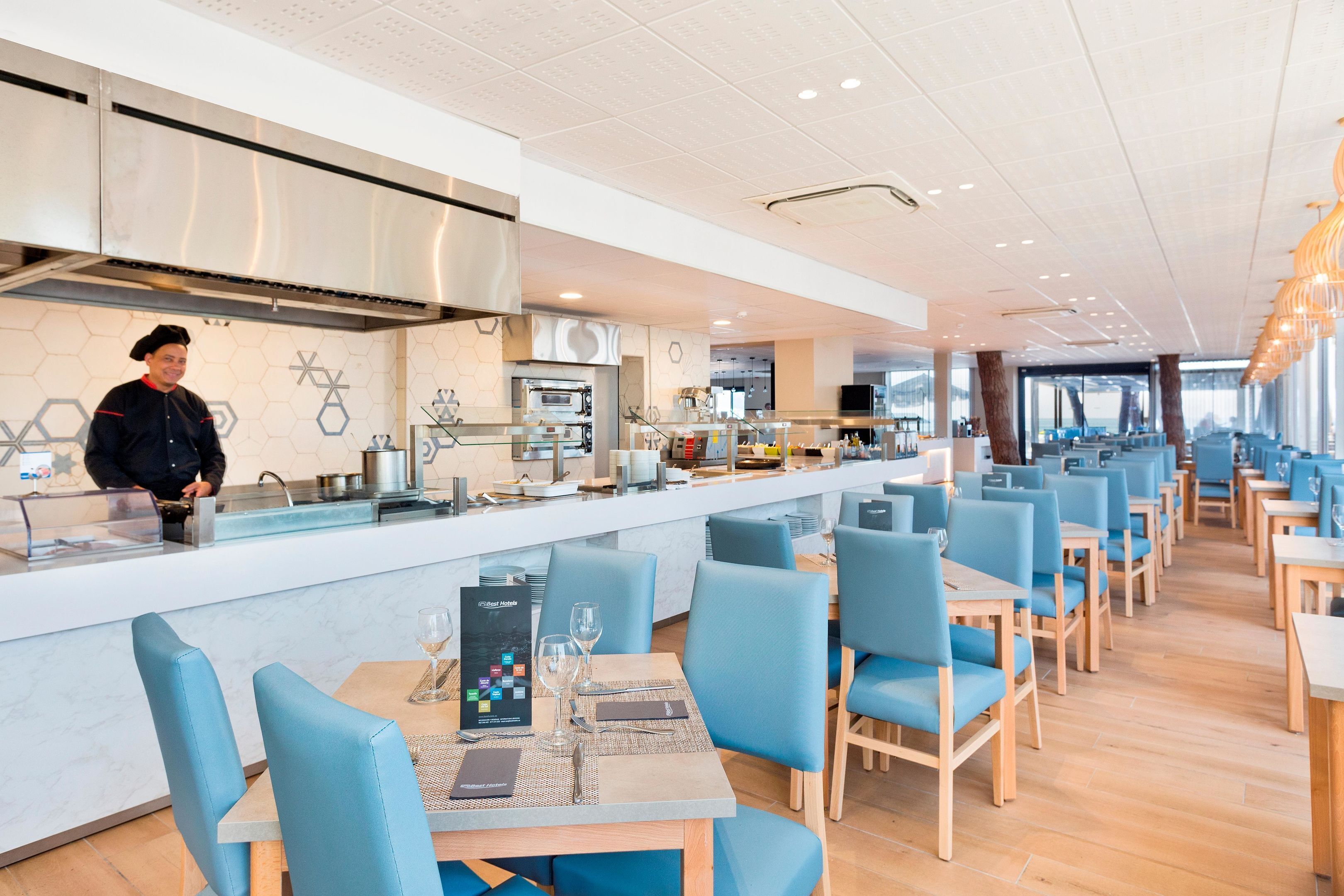 Um restaurante moderno com um balcão extenso, cadeiras azuis e um chef preparando a comida.