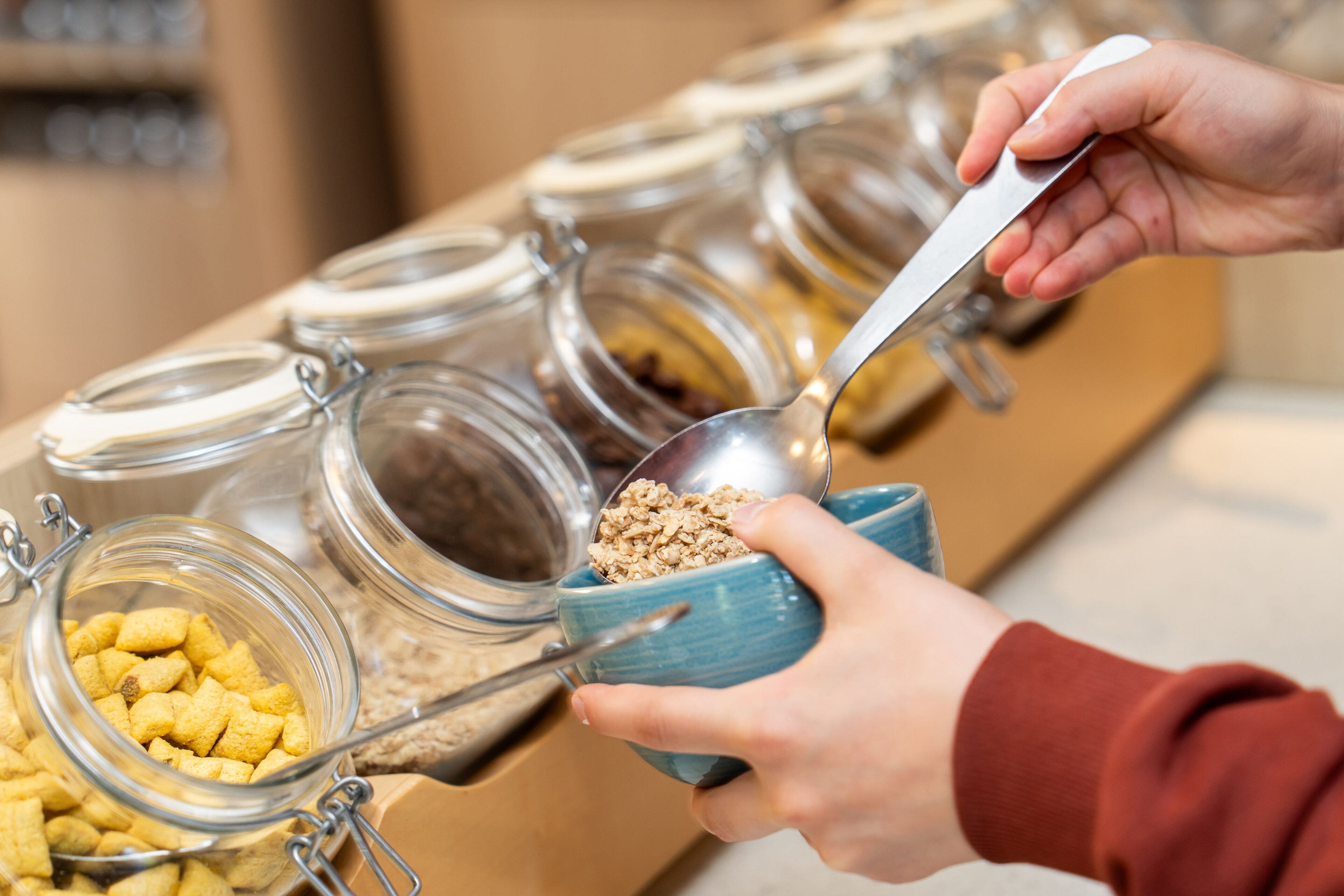 Uma pessoa escolhendo comida de um buffet com diversos itens alimentares em recipientes de vidro.
