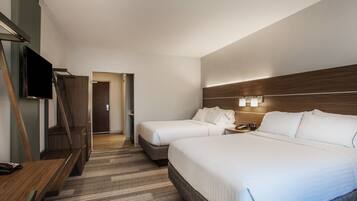 Quarto de hotel com duas camas, uma escrivaninha, uma TV e um painel de cabeceira de madeira.