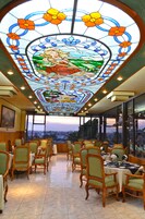 Um restaurante com um amplo teto de vitrais, cadeiras e mesas de madeira dispostas para refeições.