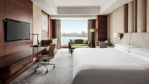 Quarto de hotel com uma cama grande, uma escrivaninha com cadeira, televisão e vista para a cidade.