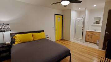Quarto com cama, mesa de cabeceira, luminária e banheiro com chuveiro e vaso sanitário.