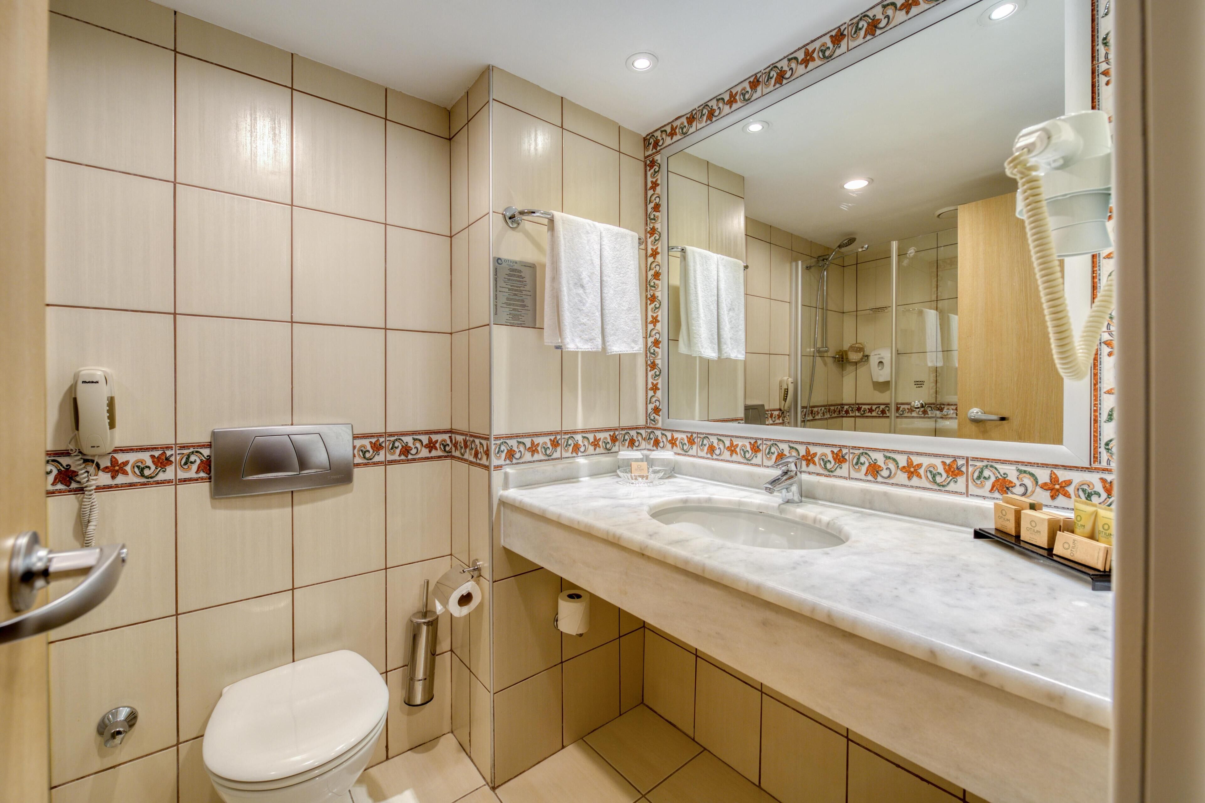 Casa de banho com sanita, duas pias, espelho e porta-toalhas.