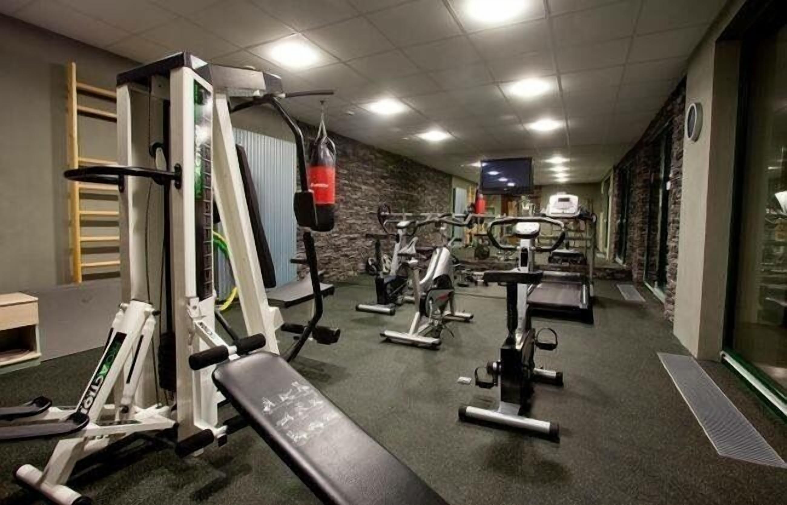 Uma academia com diversos aparelhos de exercícios, um banco e um saco de pancadas.
