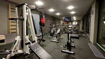 Uma academia com diversos aparelhos de exercícios, um banco e um saco de pancadas.