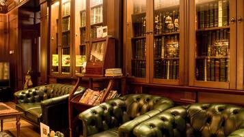 Uma biblioteca com poltronas de couro, estantes de madeira e um quadro em cima de uma mesa.