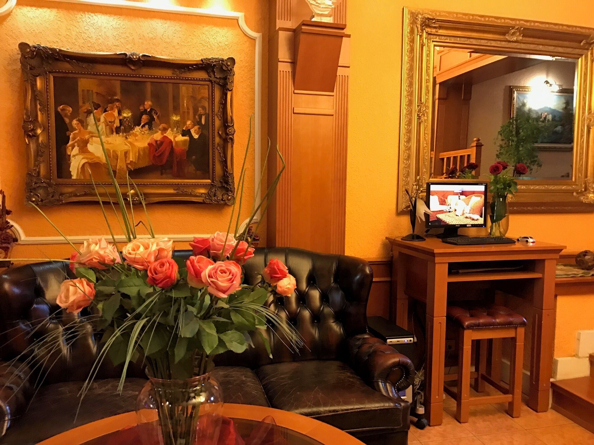 Uma sala de estar com um sofá de couro, uma mesa de centro com um vaso de flores, uma televisão sobre um suporte de madeira e duas imagens emolduradas na parede.