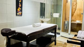 Casa de banho moderna com mesa de massagem, cabine de duche em vidro e área de sauna em madeira.