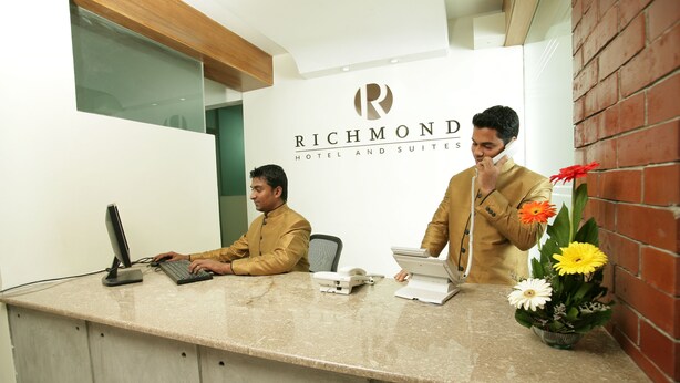 Balcão de recepção no Richmond Hotel e Suites, com um computador, telefone e um vaso de flores.